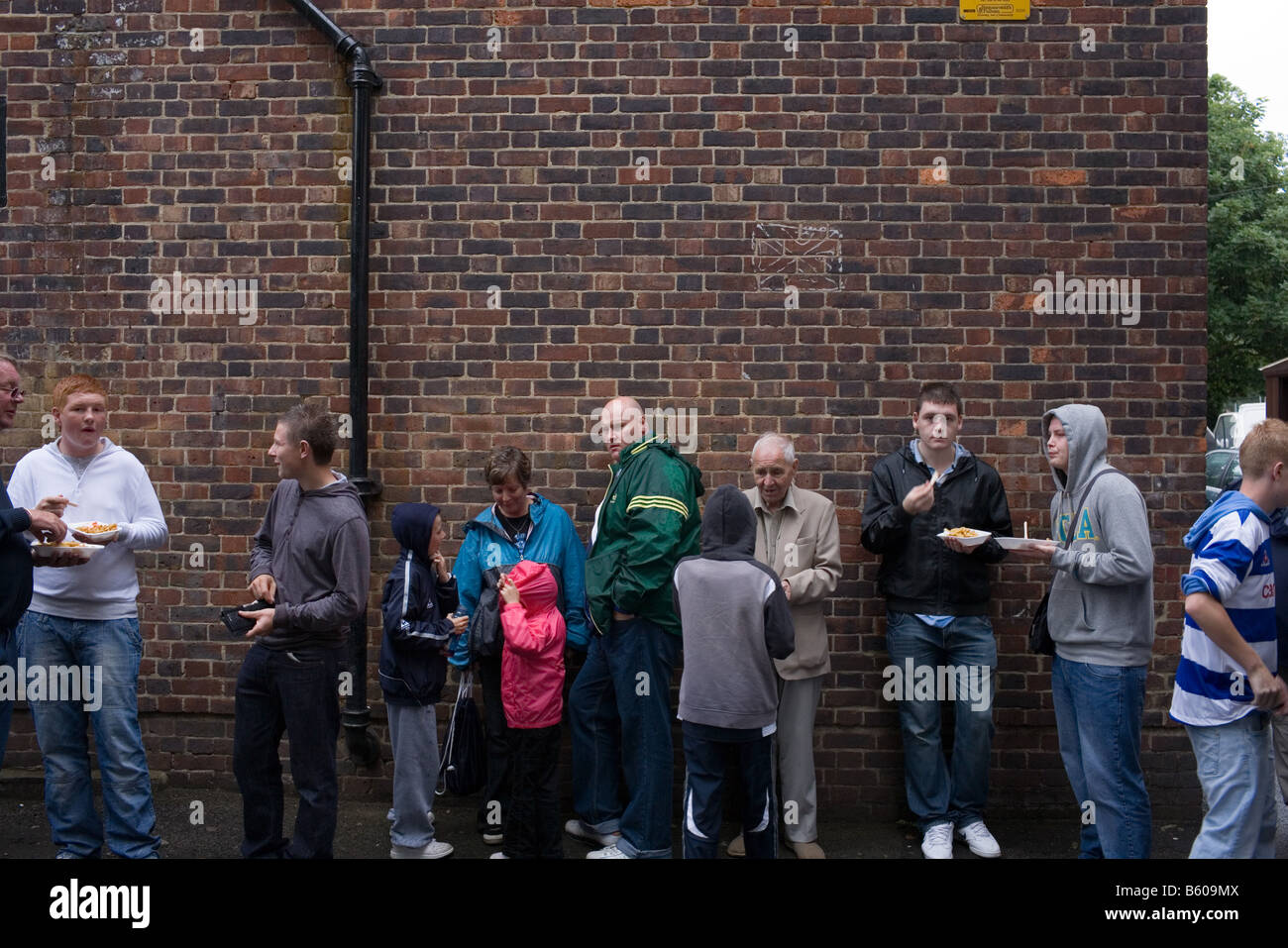A line of Football fans eat by a wall Stock Photo - Alamy