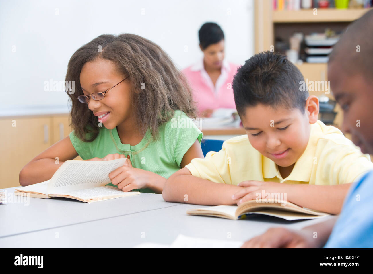 Students in class reading with teacher in background (selective focus ...