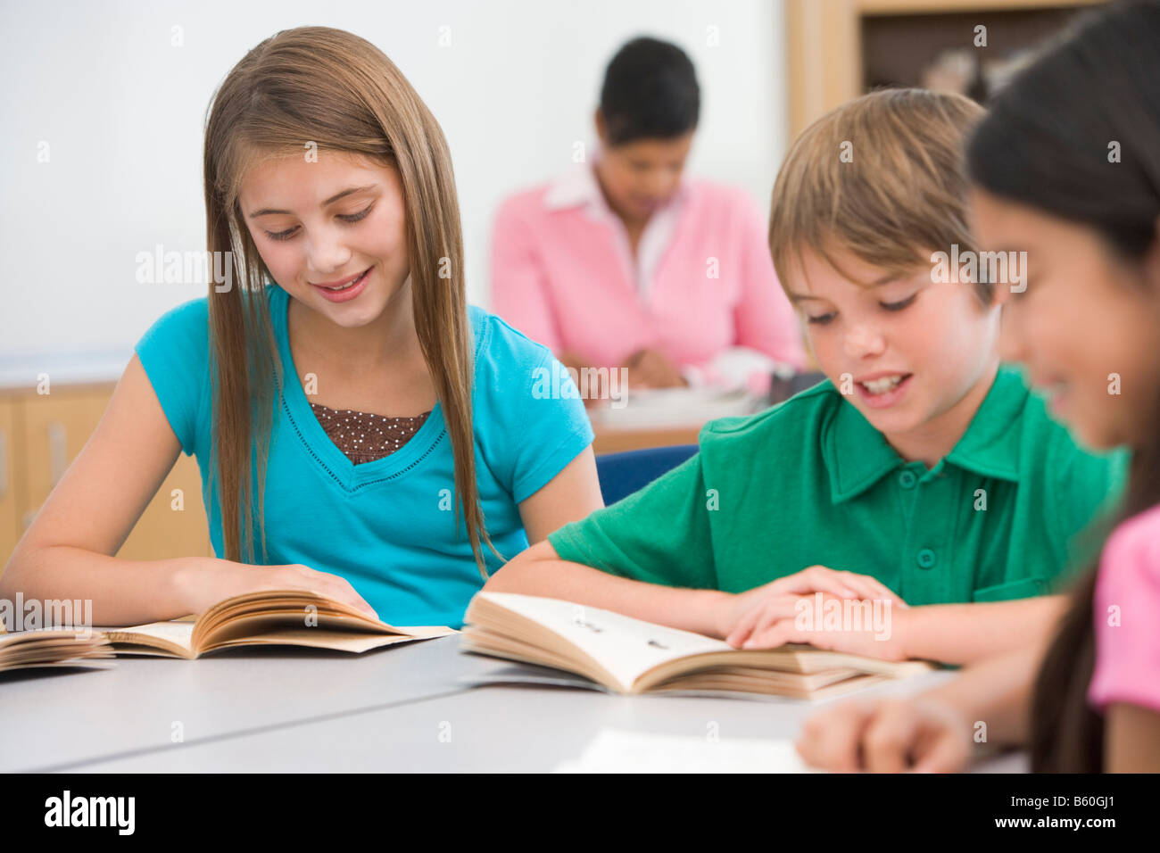 Students in class reading with teacher in background (selective focus ...