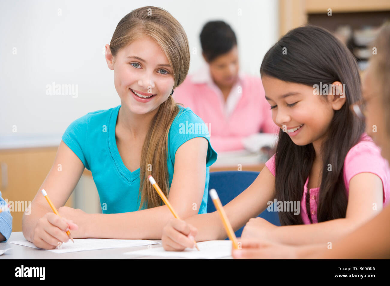 Students in class writing with teacher in background (selective focus ...