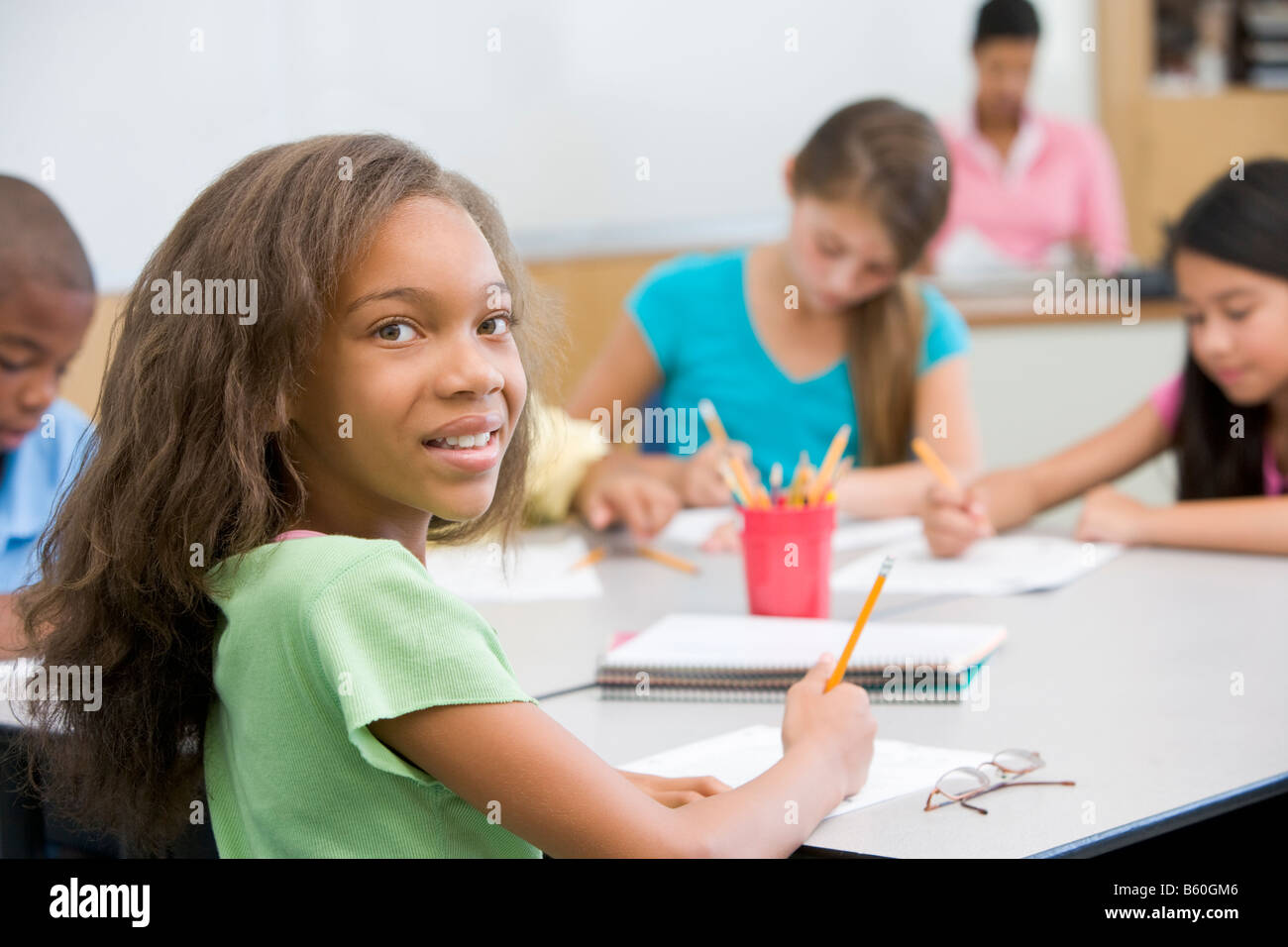 Students in class writing with teacher in background (selective focus ...