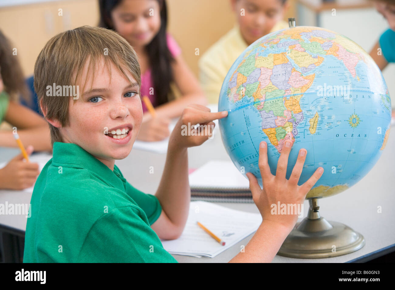 Student in class pointing at globe with students in background ...