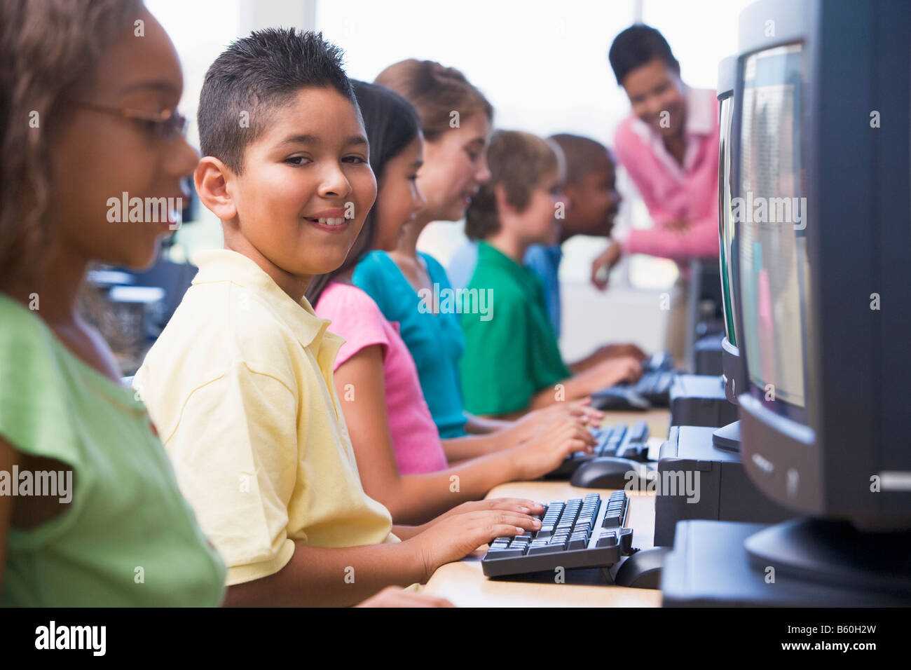 Six children at computer terminals with teacher in background ...