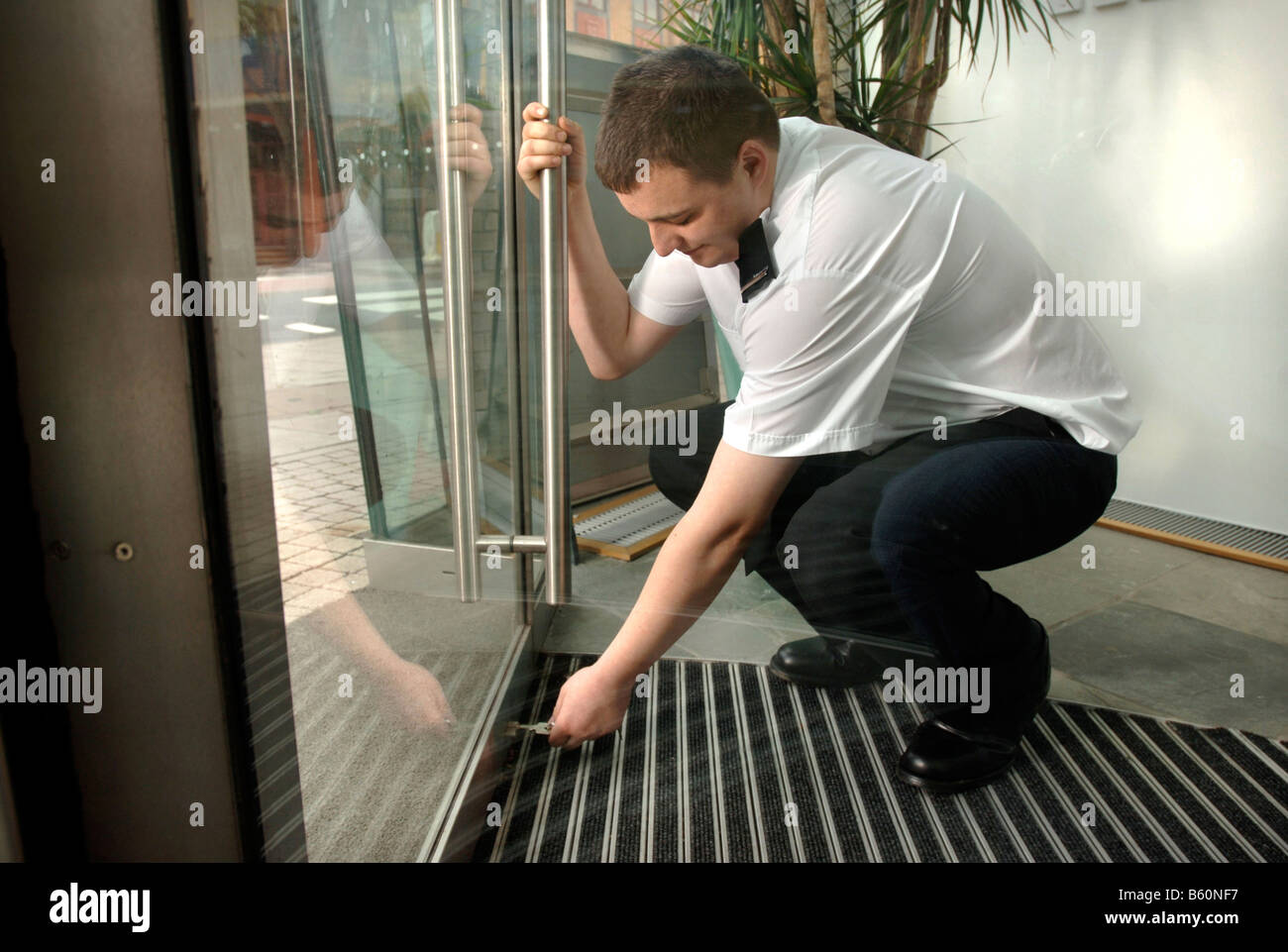 A SECURITY GUARD ON PATROL UNLOCKS THE DOOR OF A BUSINESS PREMISES UK ...