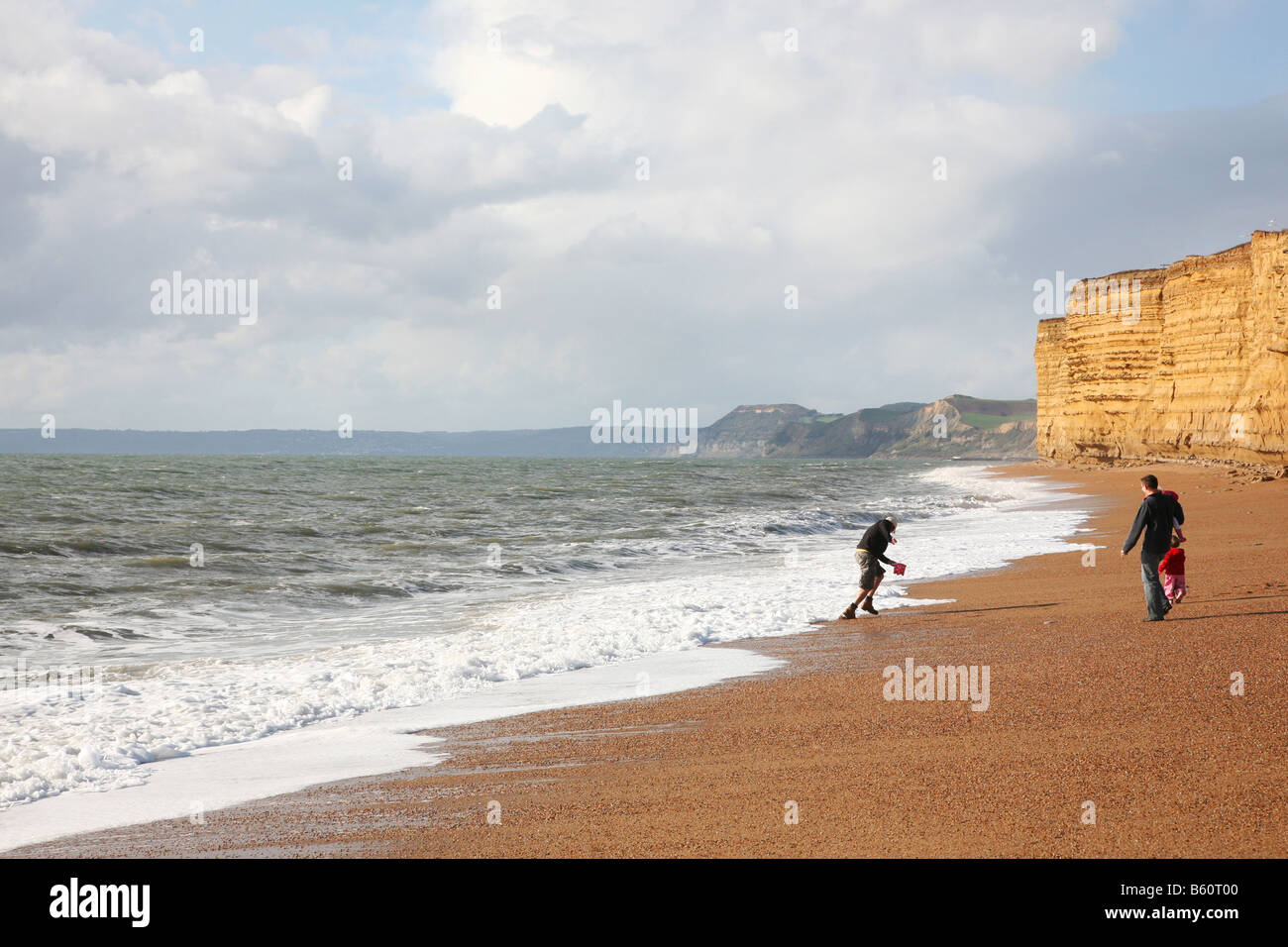People running from a wave coming onto Chesil Beach Stock Photo - Alamy
