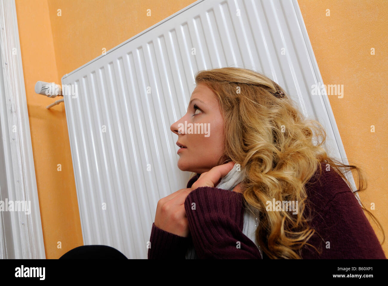 Young woman sitting in front of a radiator, freezing, symbolic picture ...