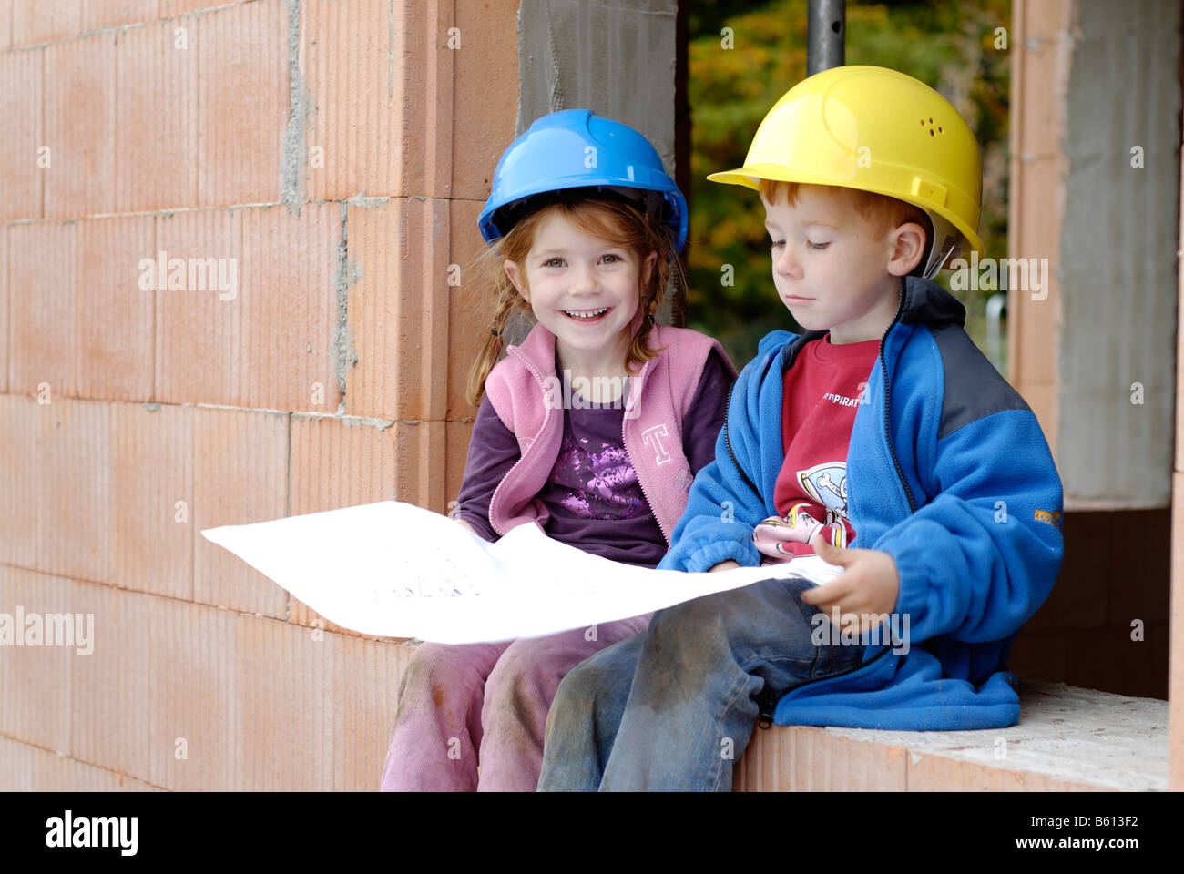 Two little children, siblings, wearing hard hats studying a building ...