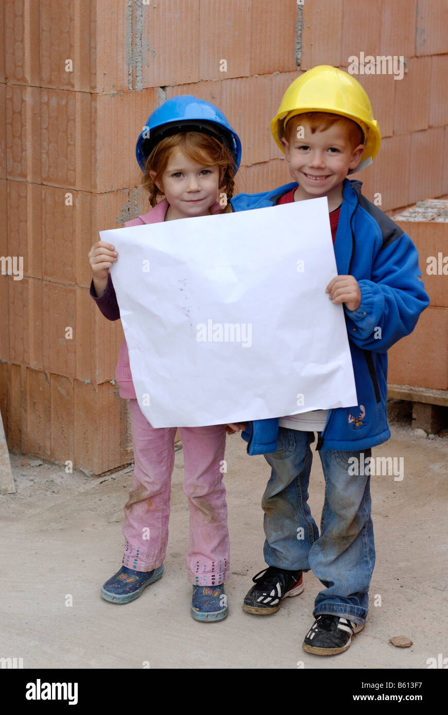 Two little children, siblings, wearing hard hats studying a building ...