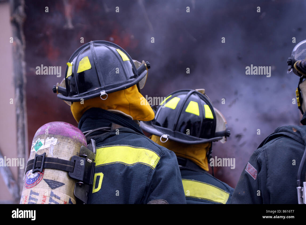 Three fire fighters surrounded by smoke while putting out a fire with a ...