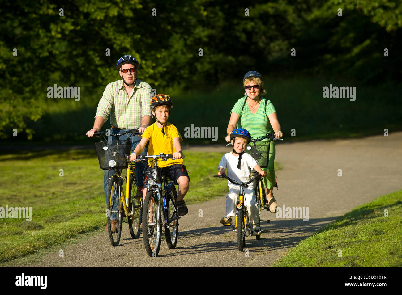 Family with 2 children riding bicycles through a park, wearing helmets ...