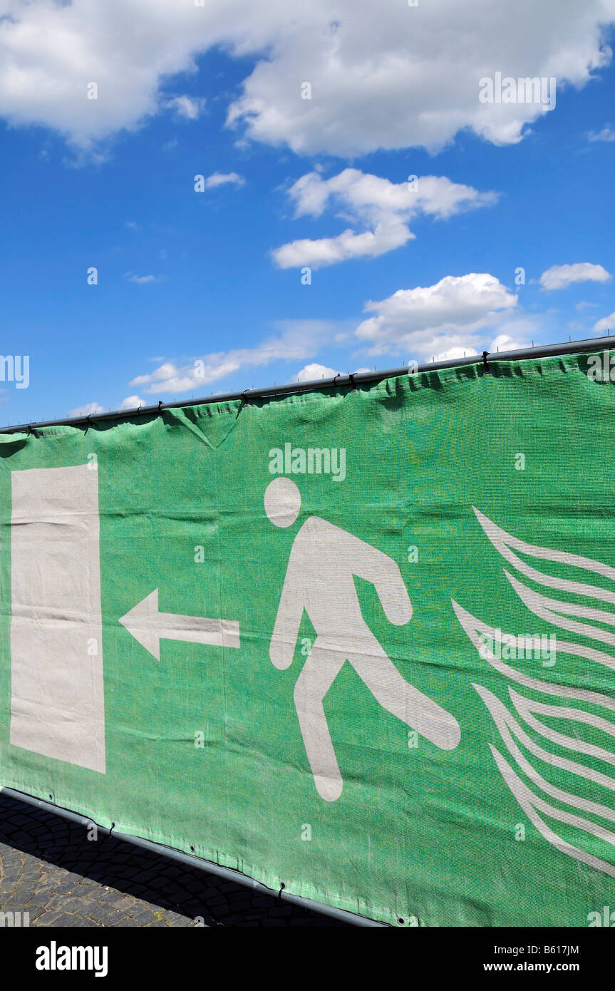 Green barrier with emergency exit motif in front of blue sky with white ...