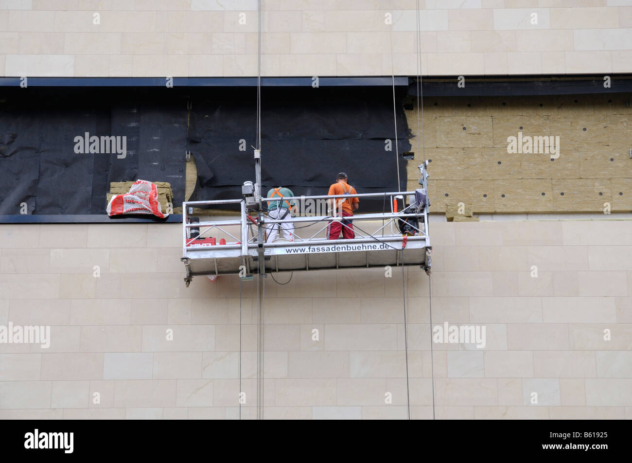 Building workers on a work platform applying insulating material ...