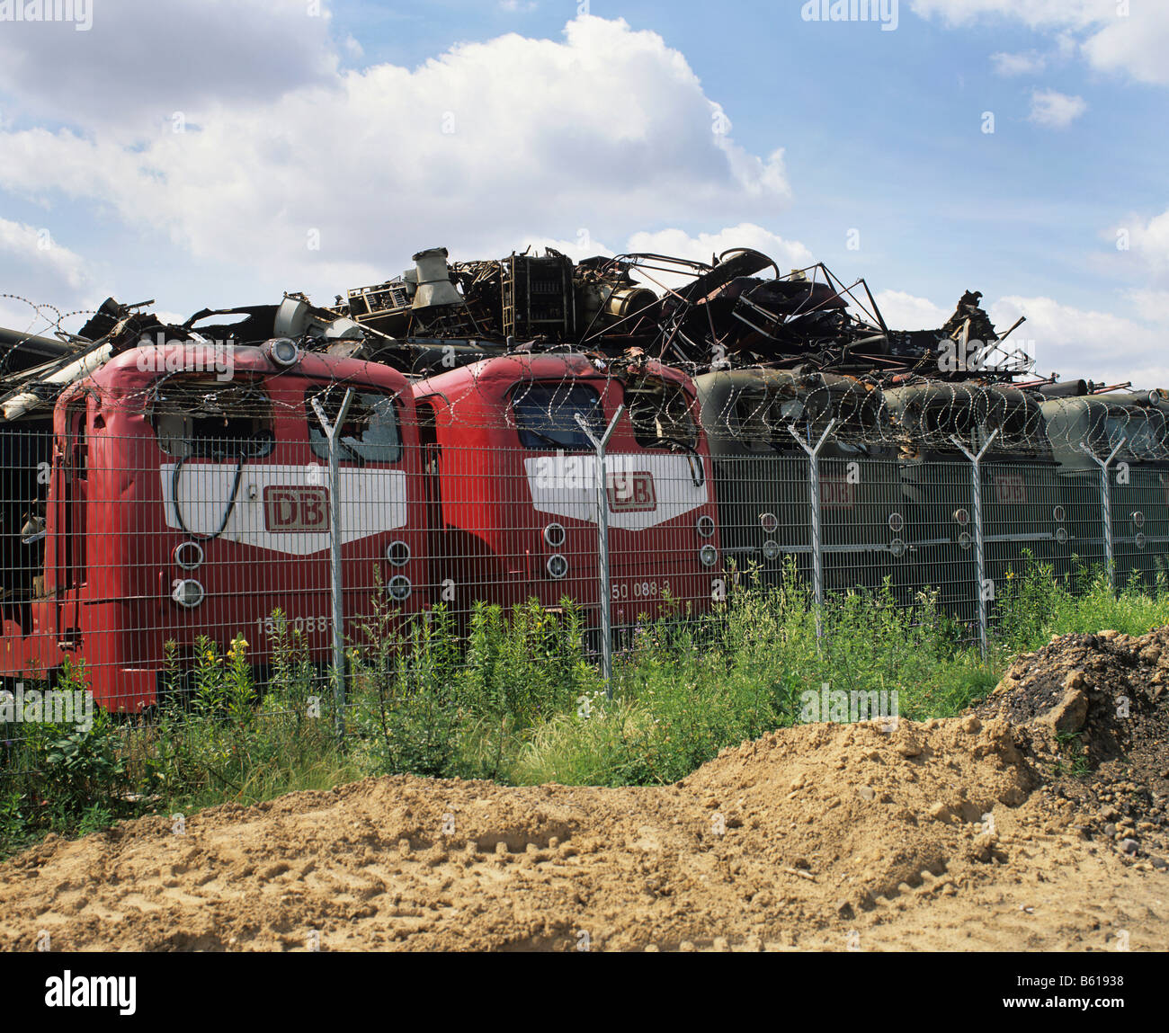 Scrapyard, electric trains and behind them piled-up old metal parts ...