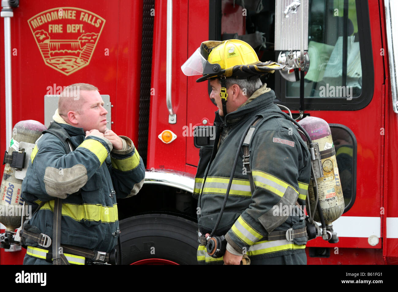 Two firefighters getting their gear on in front of a fire truck Stock ...