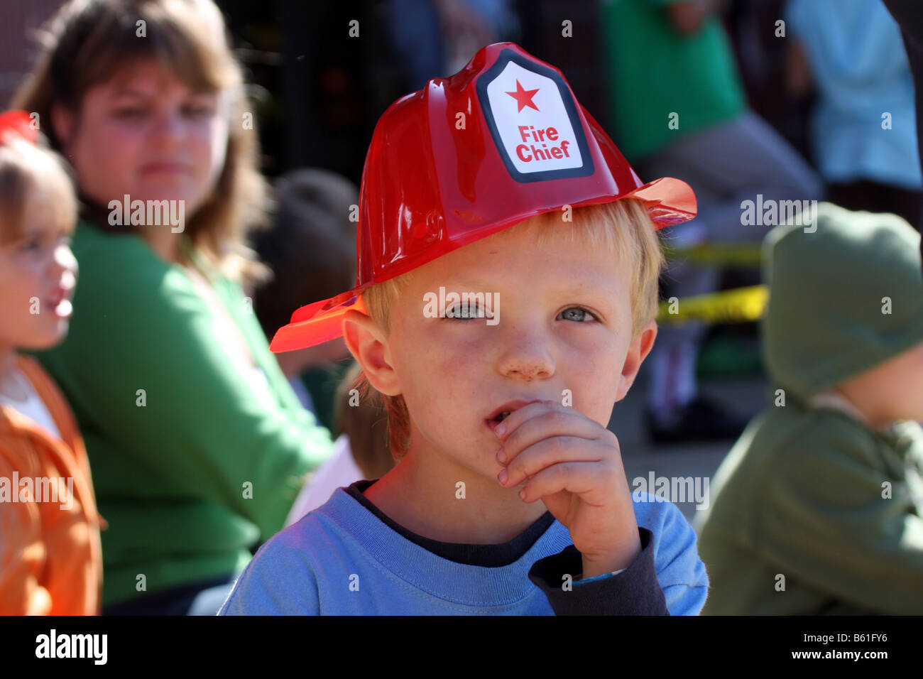 A small boy with a Fire Chief fire hat on his head in a group of people ...