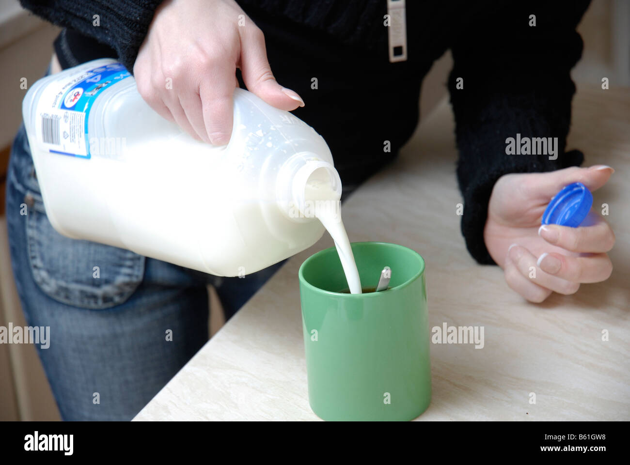 Pouring milk into a mug while making a hot drink cup of tea at home ...