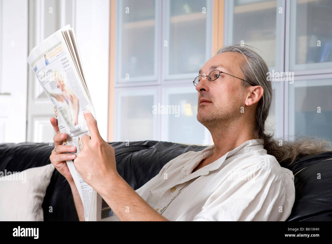 Man on a sofa reading the paper Stock Photo - Alamy