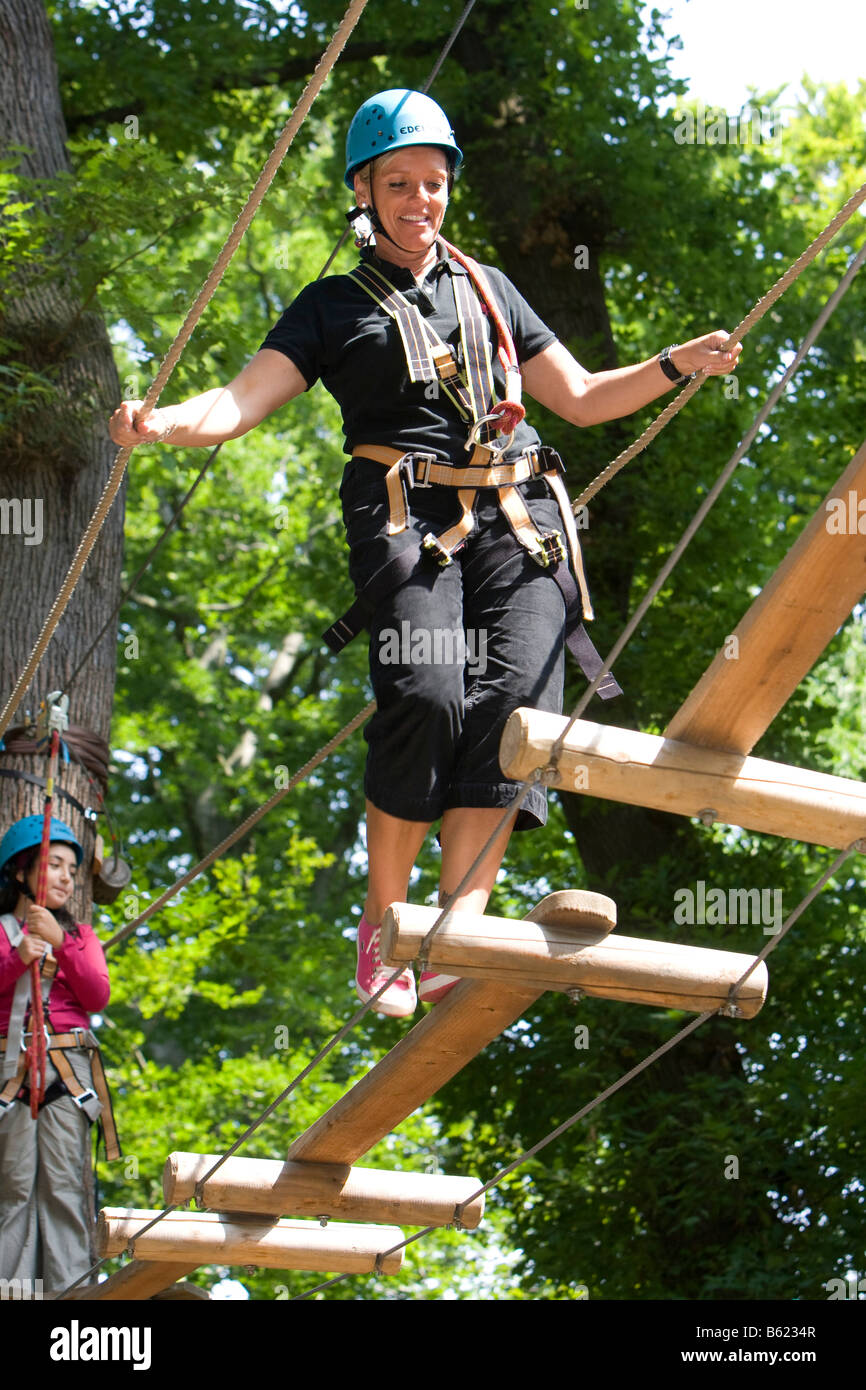 Young woman balancing on a wooden beam strung between two trees ...
