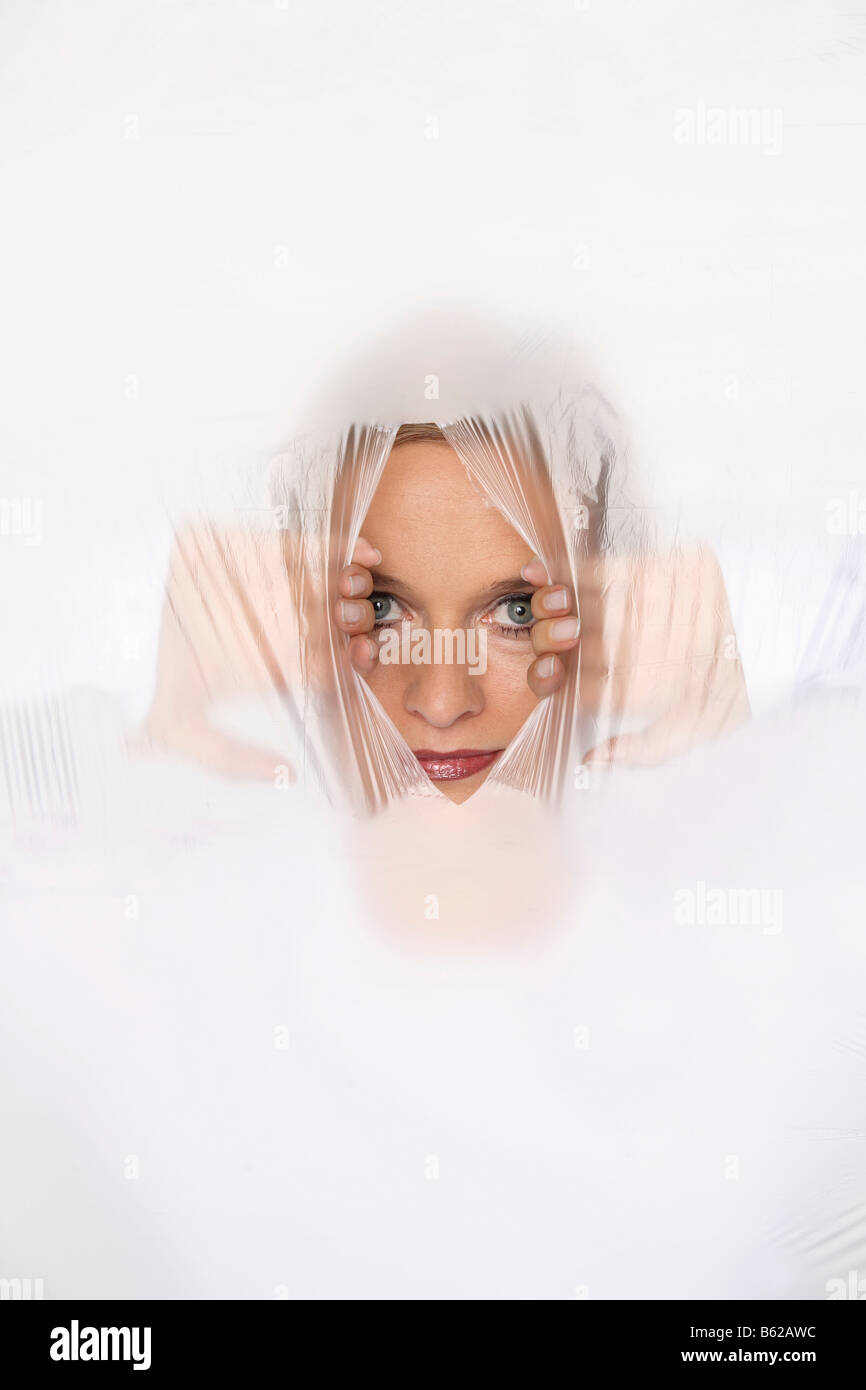 Young woman tearing a hole in a plastic sheet, looking through Stock ...