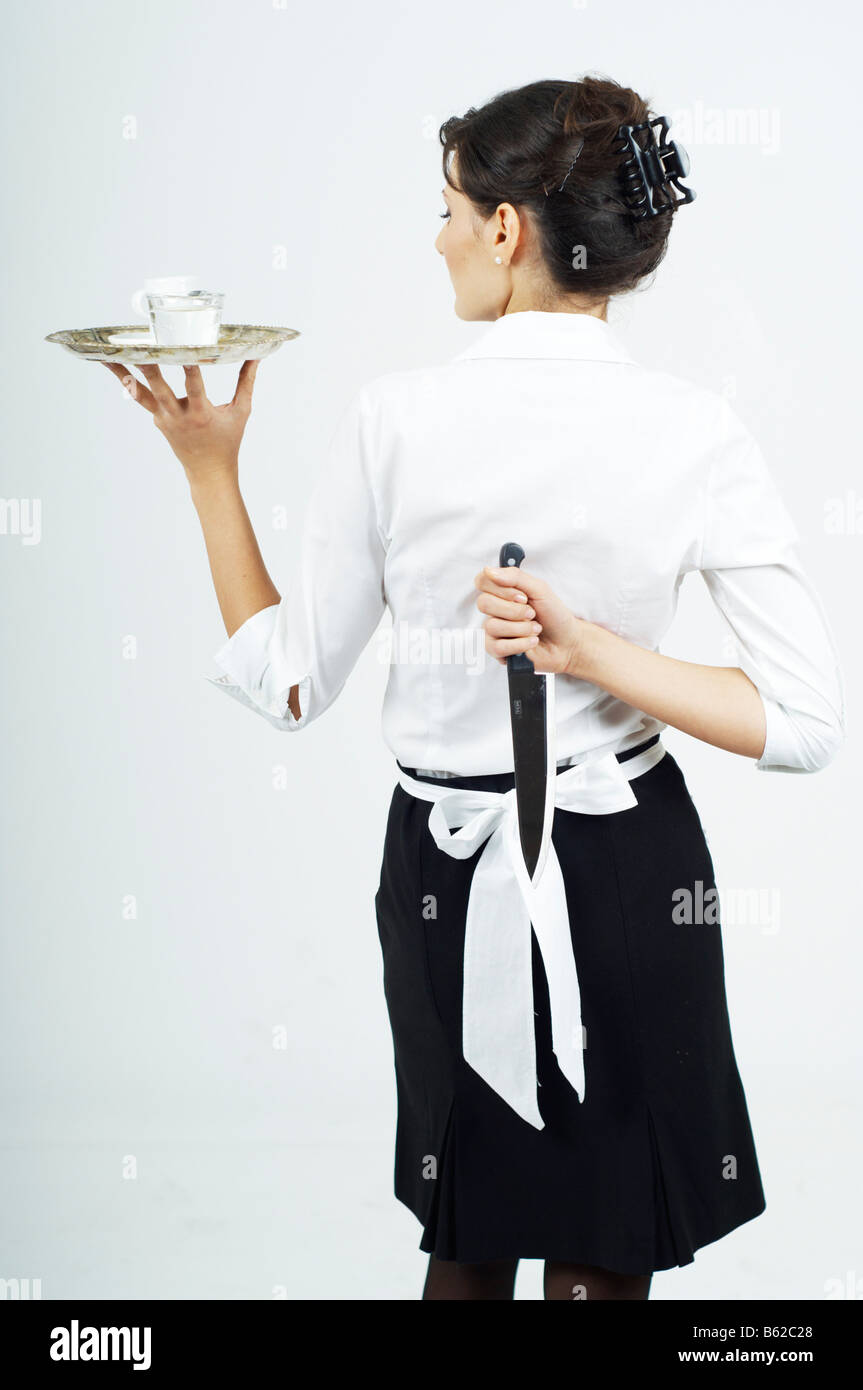 Young woman dressed as a waiter holding a long knife behind her back ...