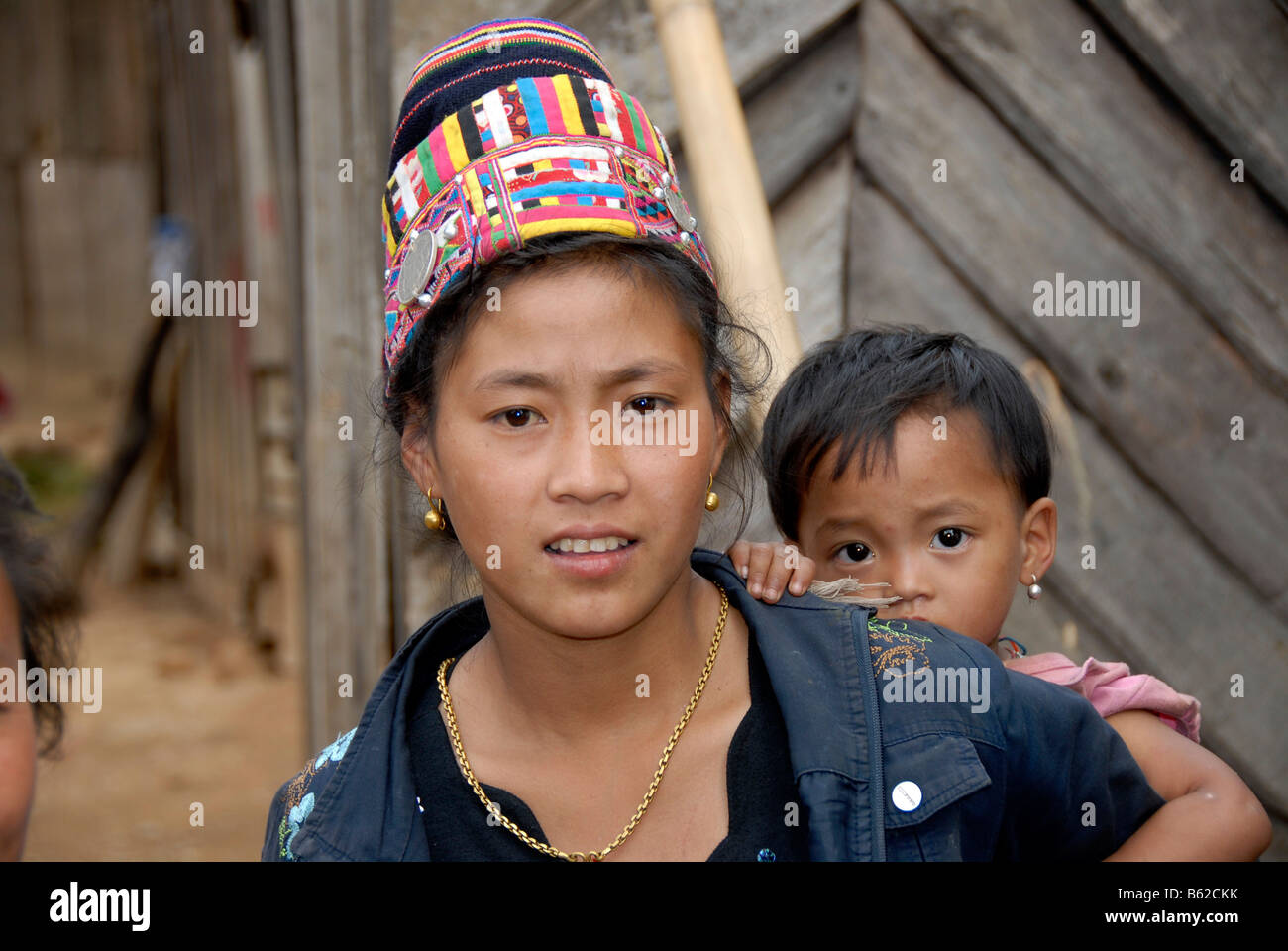 Young woman of the Akha Lom ethnic group carrying a child on her back ...