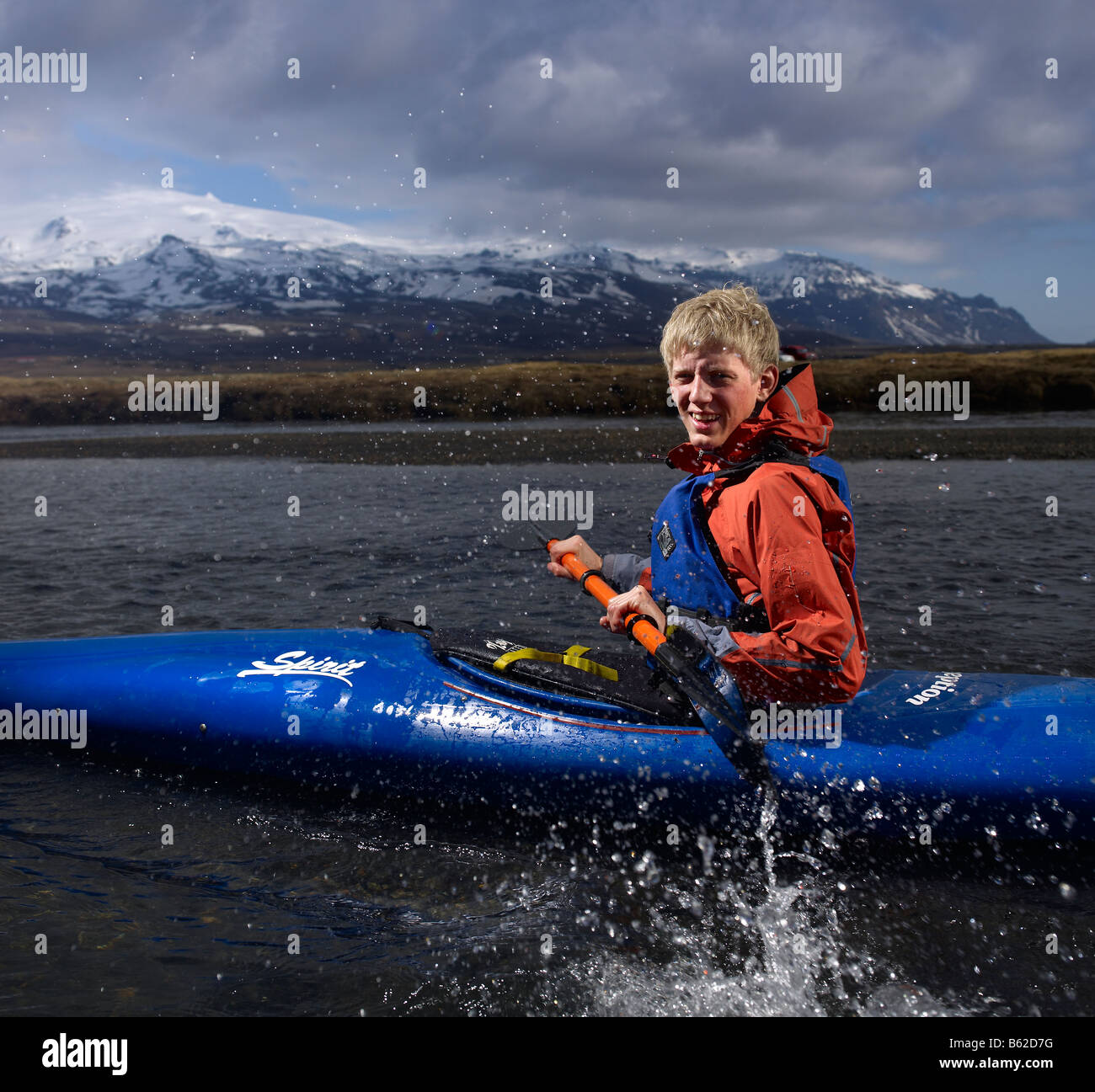 Teenage boy kayaking in river with Oraefajokull glacier in background ...
