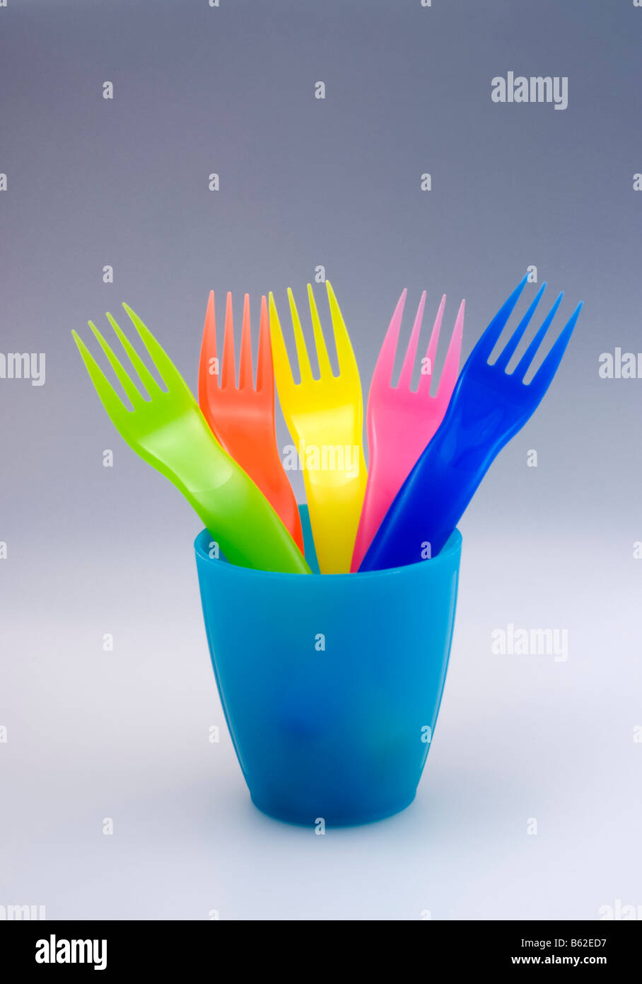 Five brightly coloured plastic picnic forks in a blue tumbler against a ...