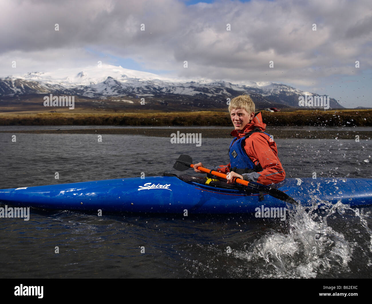 Teenage boy kayaking in river with Oraefajokull glacier in background ...