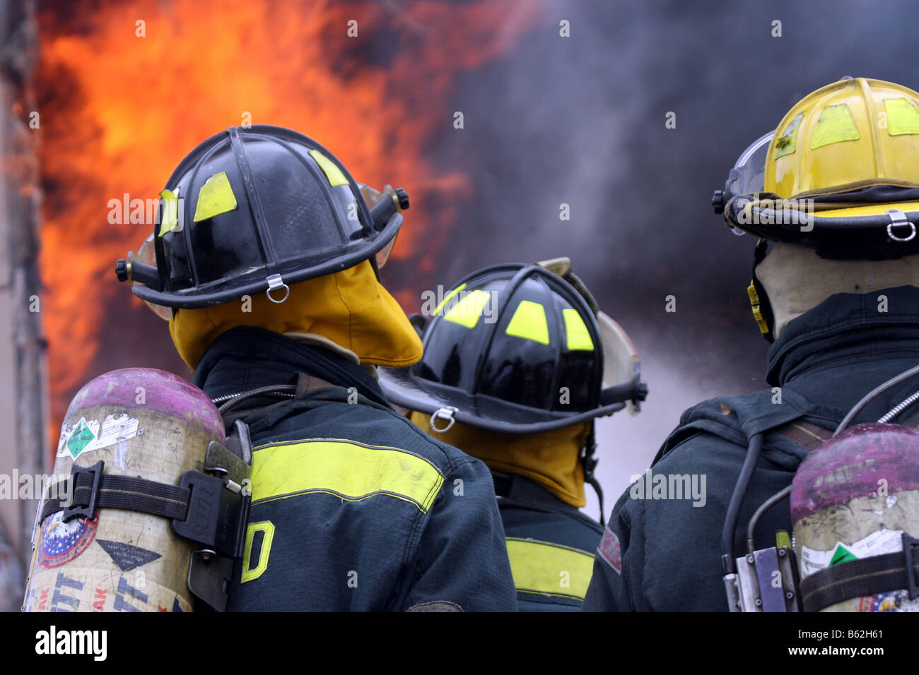 Three fire fighters surrounded by smoke while putting out a fire with a ...