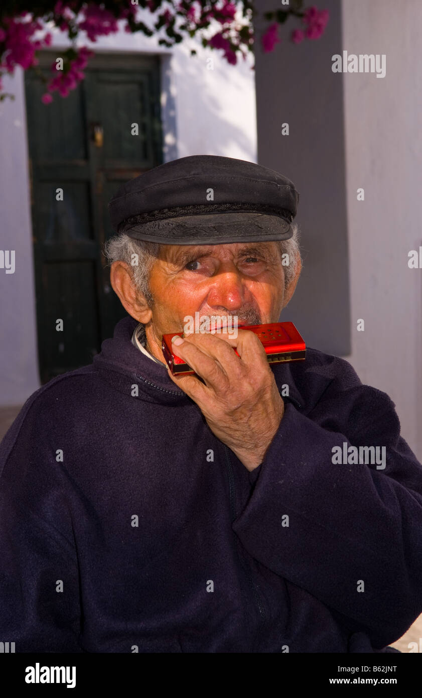 Old local man playing harmonica in beautiful village of Oia in ...
