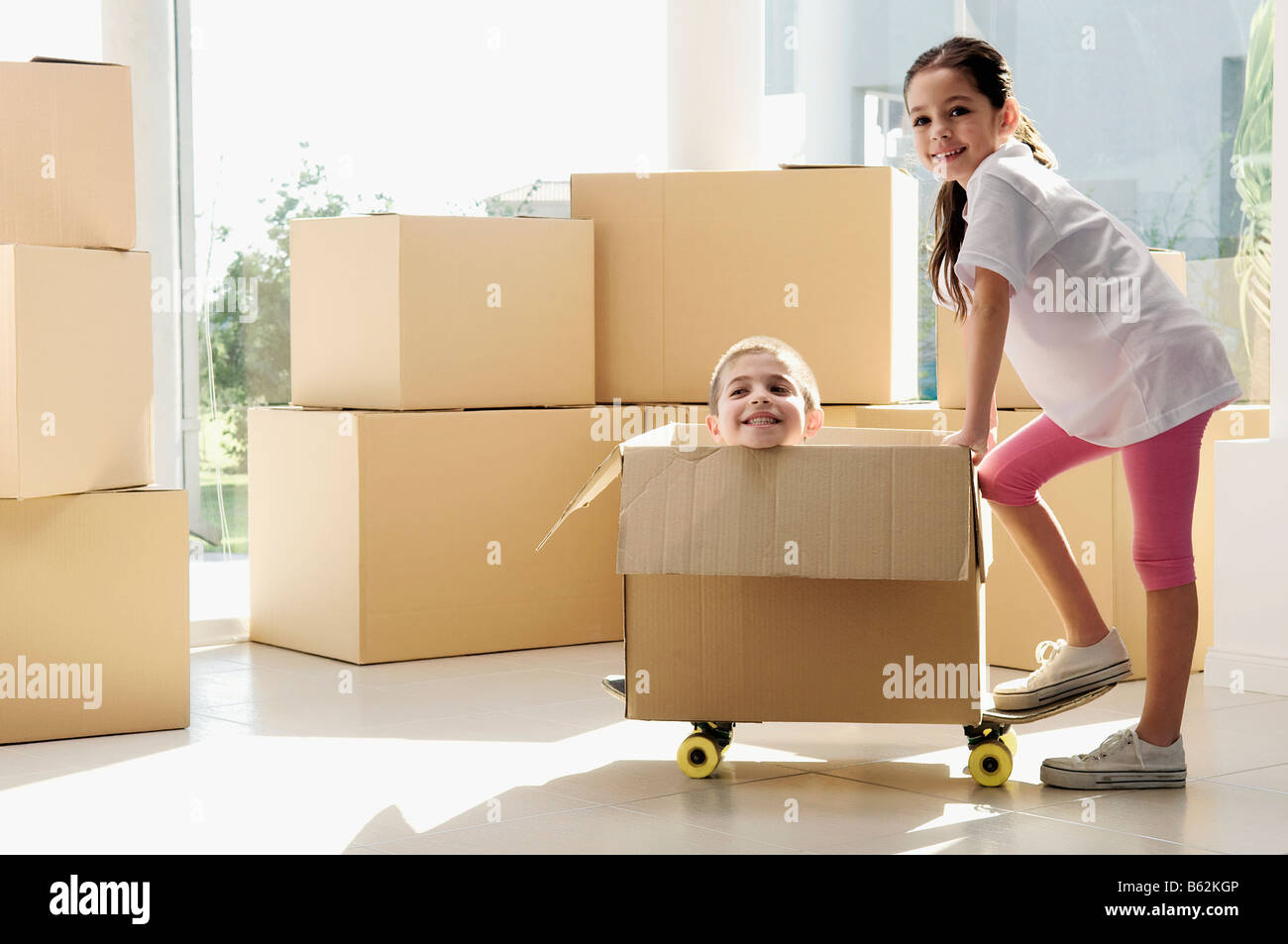 Side profile of a girl pushing a cardboard box with her brother Stock ...