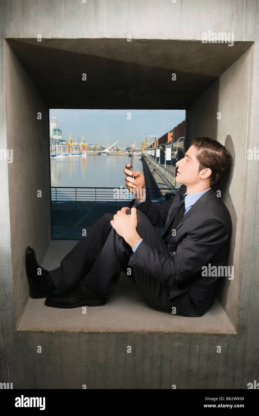 Side profile of a businessman sitting on a window sill and operating a ...