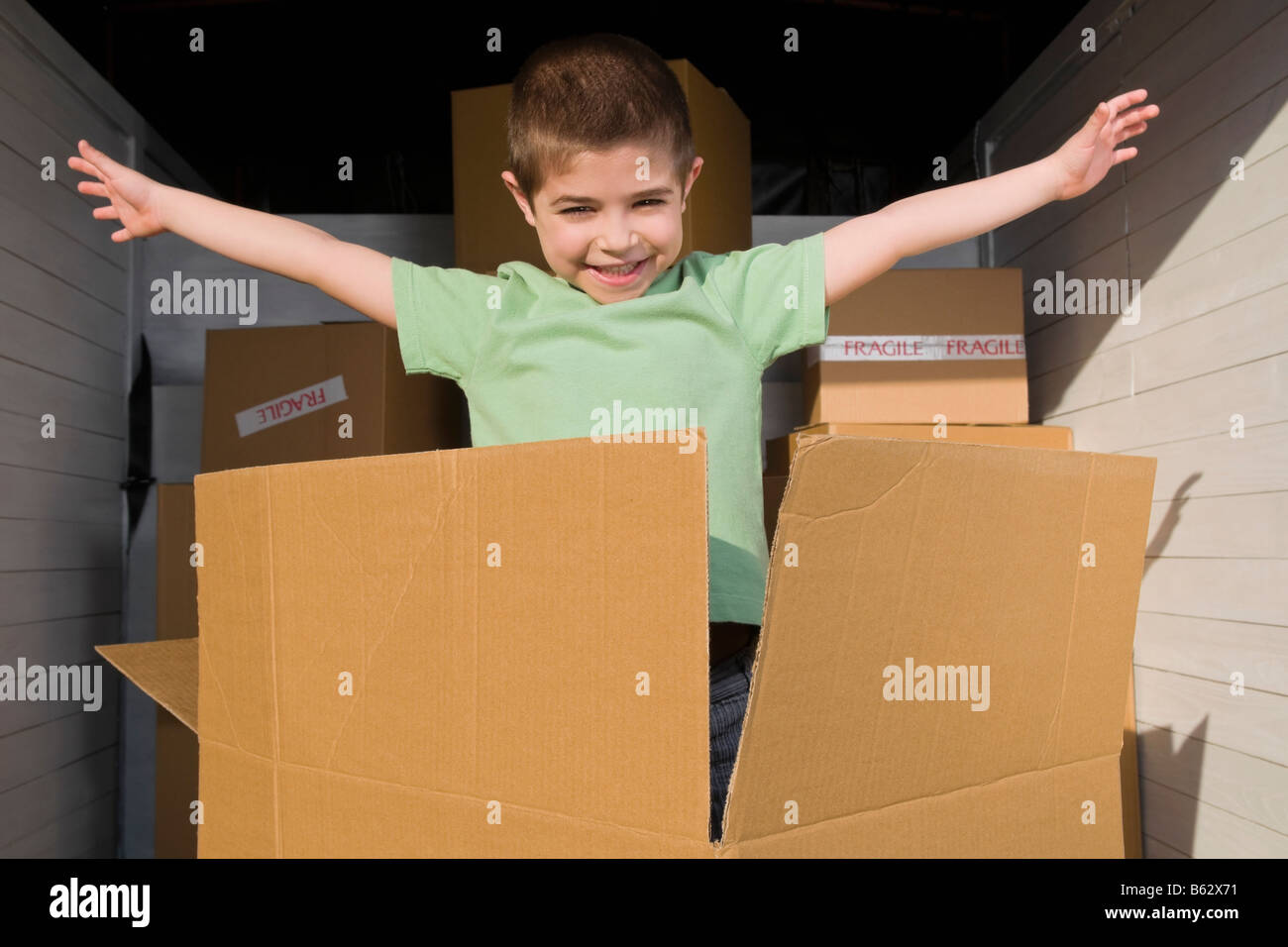 Portrait of a boy standing in a cardboard box with his arm outstretched ...