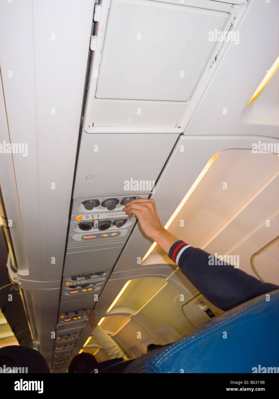 A passenger adjusting air vent on overhead control panel inside an ...