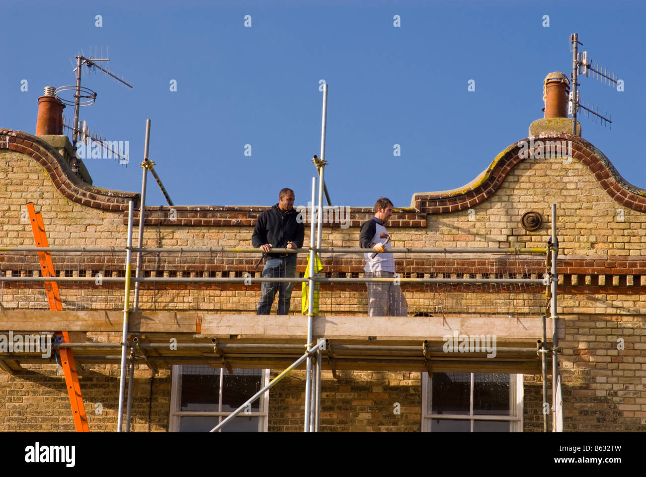Two builders pointing up the brickwork on a building standing on ...