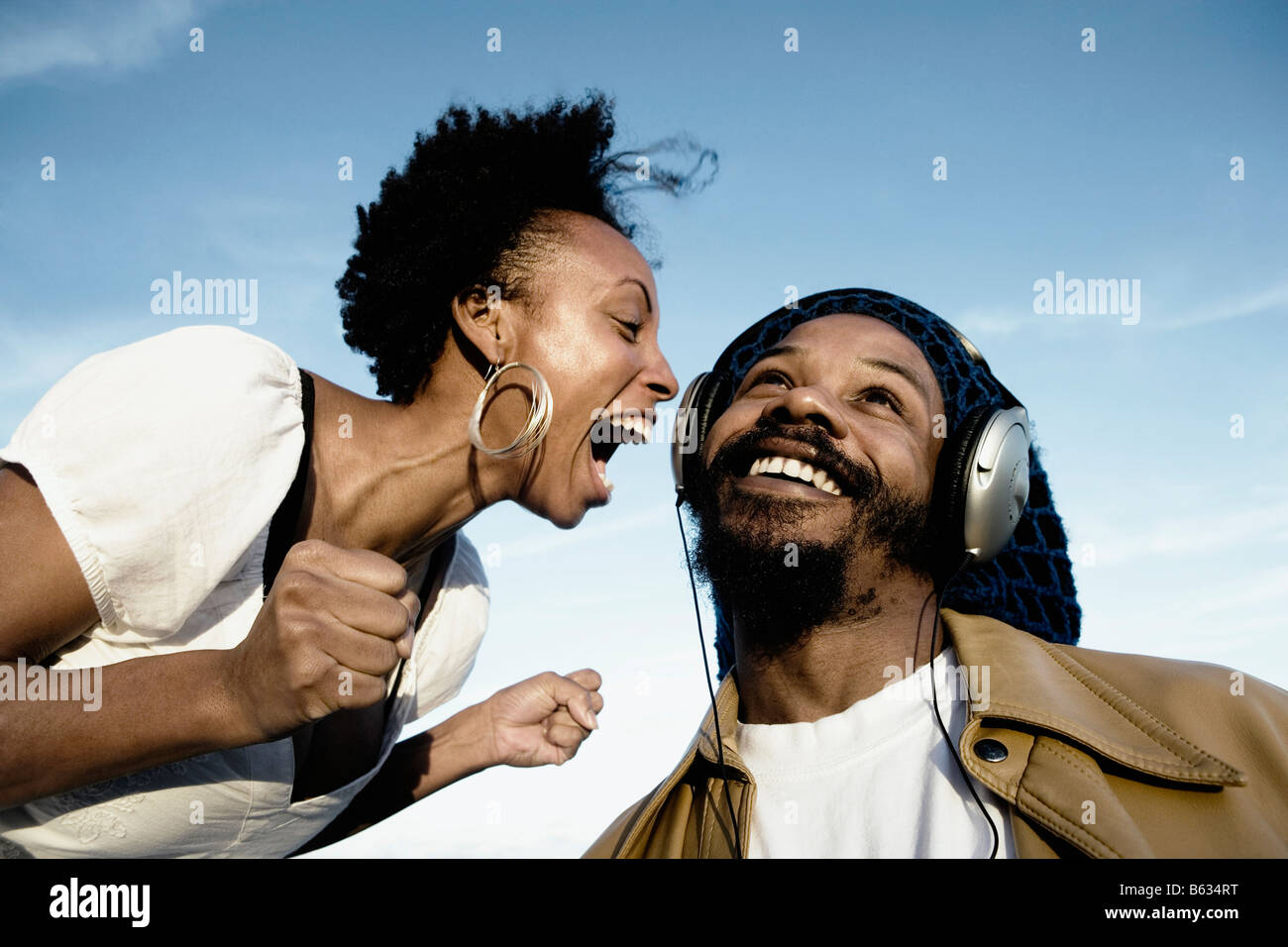 Mid adult man listening to music and a young woman shouting in front of ...