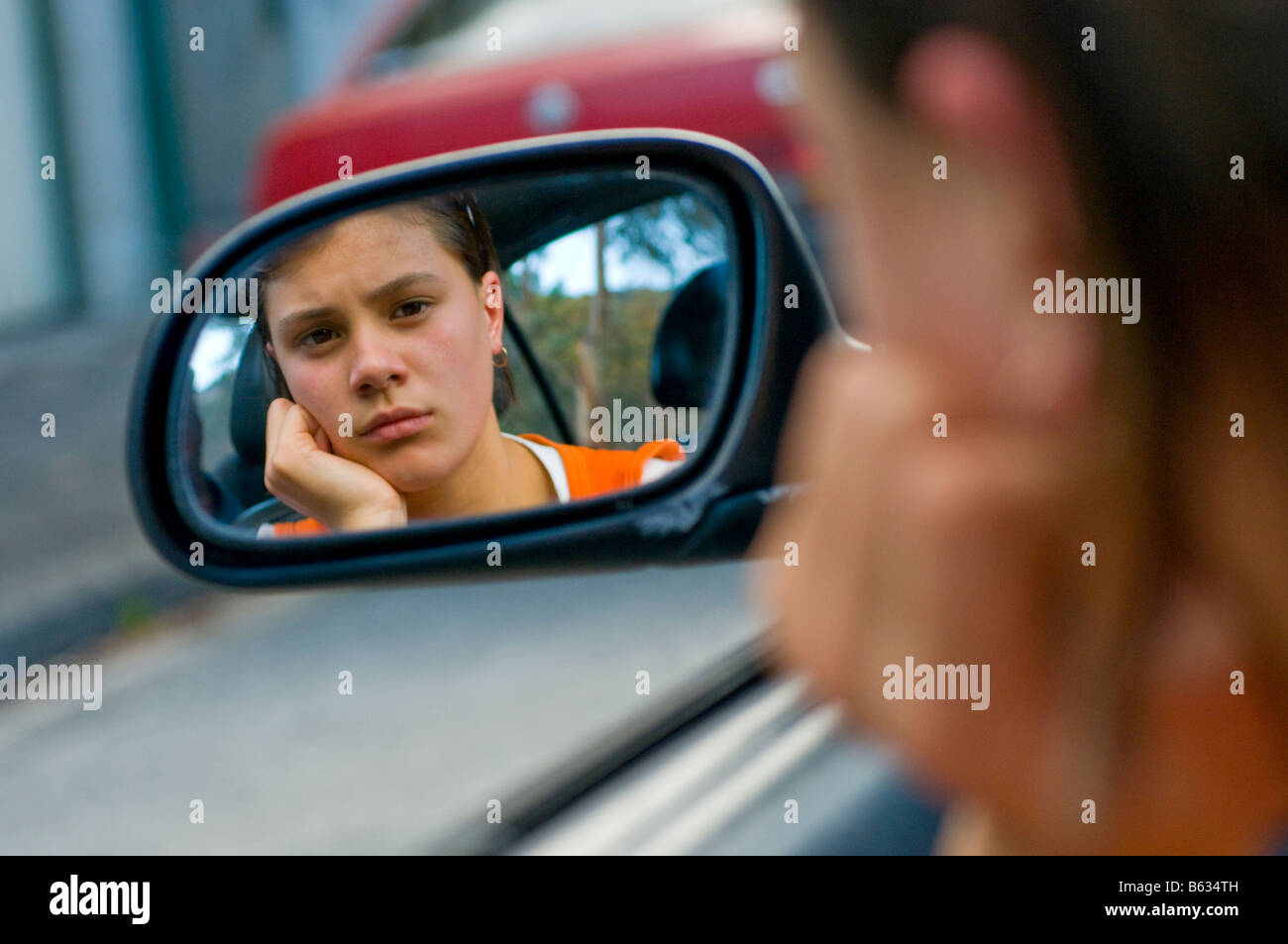 Morose young teenaged girl staring into rear-view mirror of car Stock ...