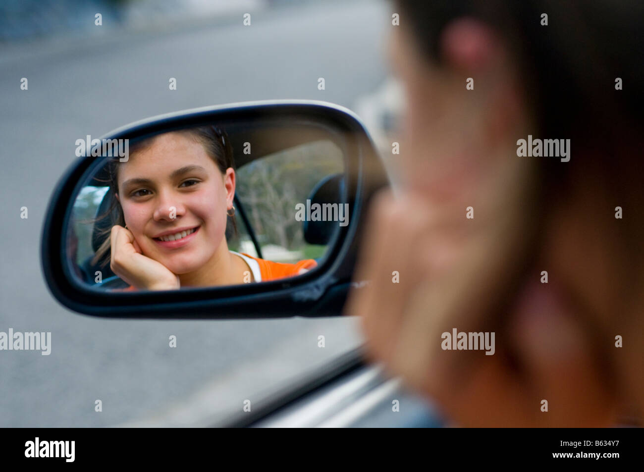 Smiling young teenaged girl looking into rear-view mirror of car Stock ...
