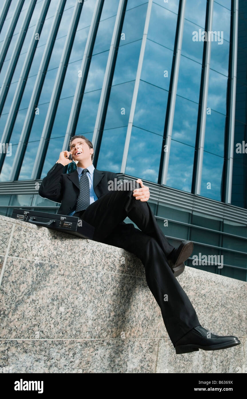 Low angle view of a businessman sitting at the edge of a wall and ...