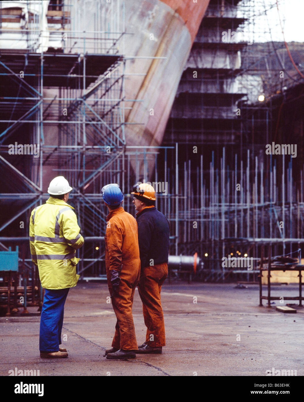 a picture of 3 men working in a dry dock looking at the bow of a ship ...