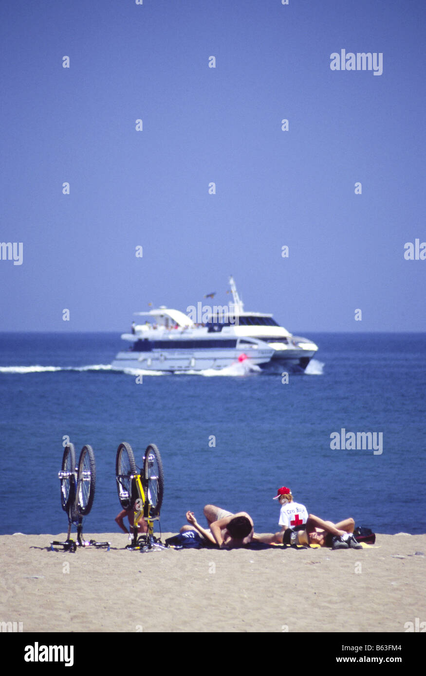 Sunbathing men lying on Barceloneta beach next to upturned bicycles ...