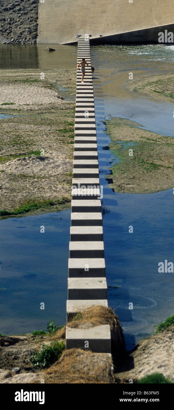 Boy leaps acros concrete blocks across river Stock Photo - Alamy