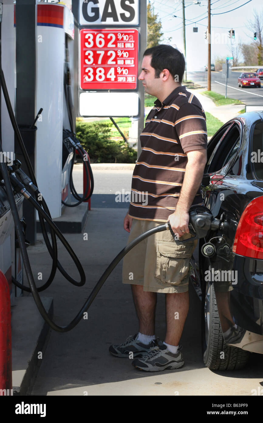 A man pumping high priced gas into his car with a disgusted look on his ...