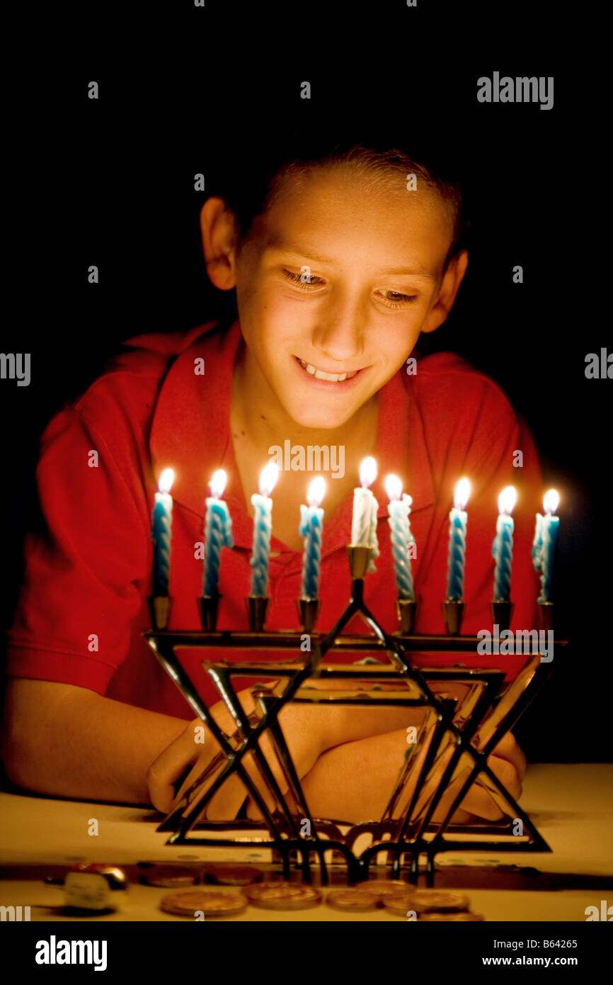 Little boy gazing on a lighted menorah illuminated only by its light ...