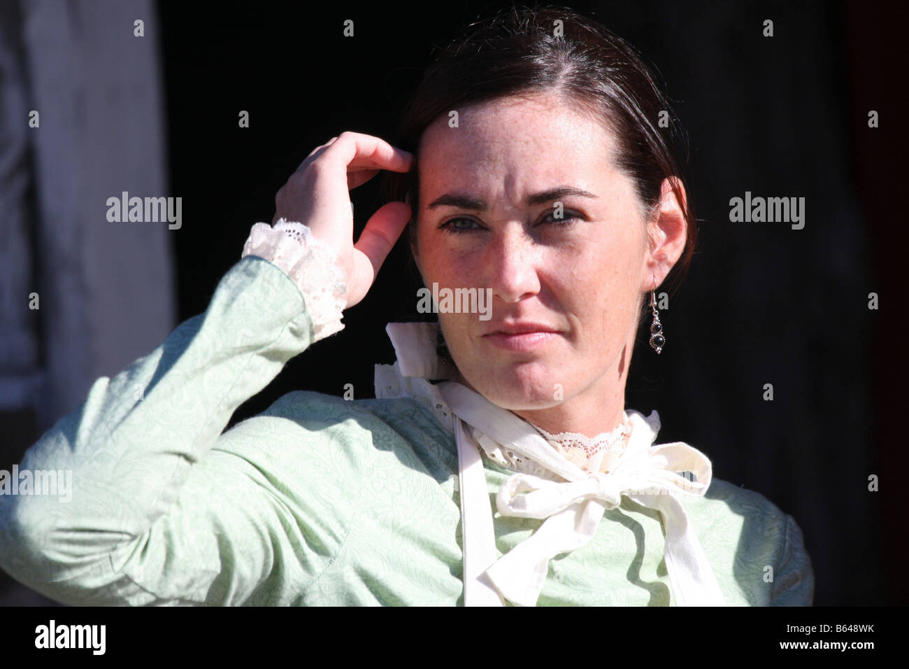 A young woman in a prairie western dress wiping the hair from her face ...