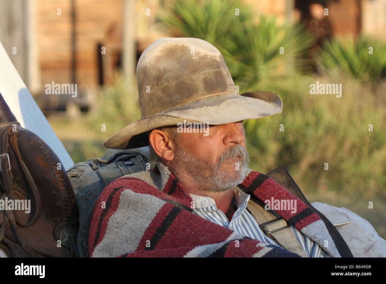 An old timer cowboy leaning against his pack and saddle Stock Photo - Alamy