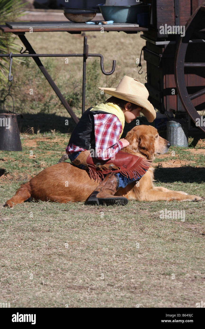 A young boy riding a Golden Retriever dog like a horse by the chuck ...
