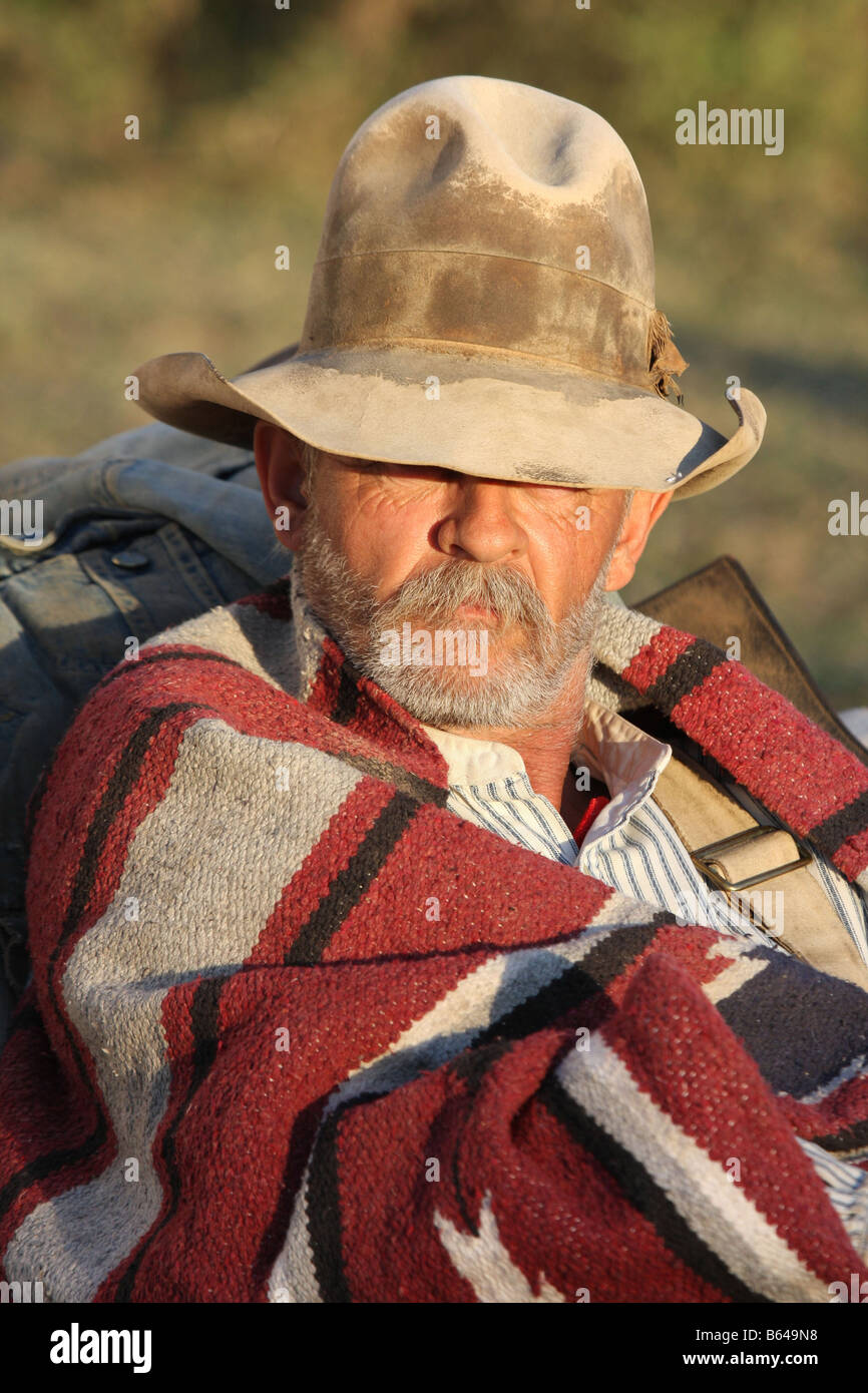 An old timer cowboy leaning against his pack and saddle next to the ...