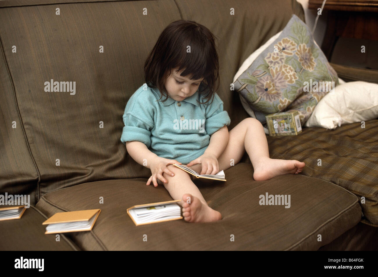 two year old girl looking at books seated on the coach Stock Photo - Alamy