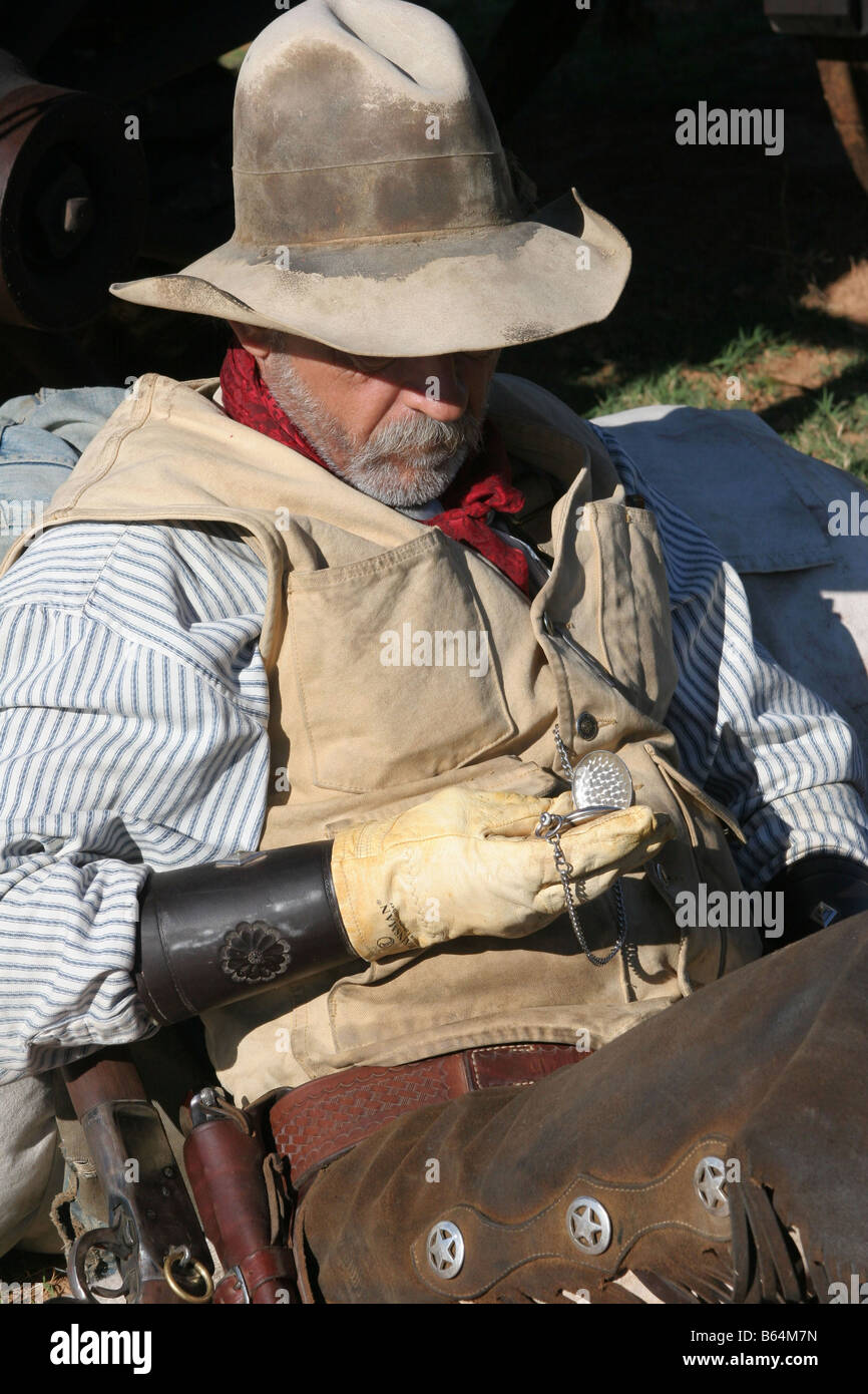 An old timer cowboy leaning against his pack checking his pocket watch ...